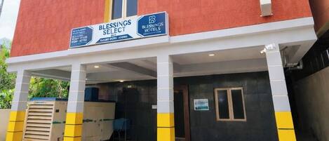 Um hotel de dois andares com fachada em vermelho e bege, entrada coberta e pilares amarelos.