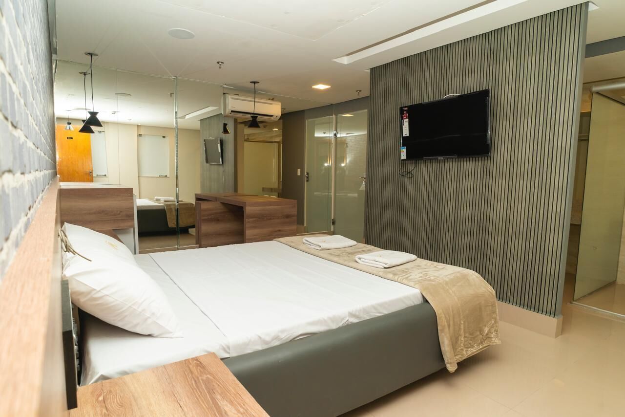 Quarto de hotel moderno com uma cama grande, uma mesa, um espelho e uma TV na parede.