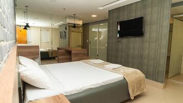 Quarto de hotel moderno com uma cama grande, uma mesa, um espelho e uma TV na parede.