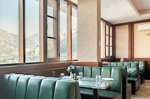 Um restaurante com bancos e mesas verdes, amplas janelas com vista para a montanha e uma parede com textura.