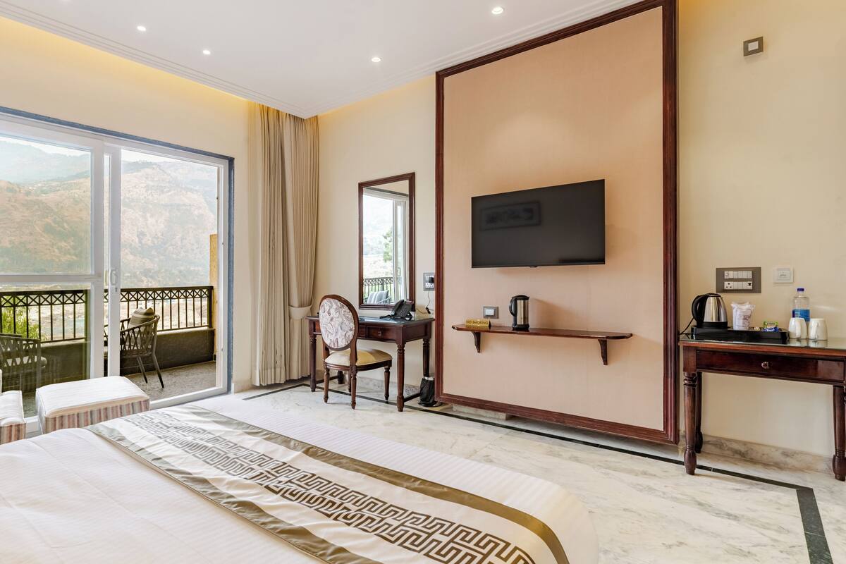 Quarto de hotel com cama, escrivaninha, televisão, varanda e cafeteira.