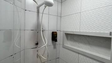 Área de chuveiro com chuveiro manual, painel de controle e uma prateleira pequena.