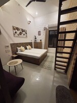 Quarto com cama, mesinha, cadeira, guarda-roupa e um objeto decorativo na parede.