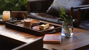 Uma mesa de madeira com uma vela, um tabuleiro com comida, um copo de água e um caderno.