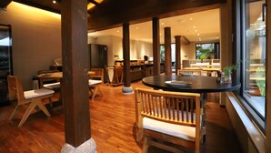 Um restaurante com mobiliário de madeira, uma mesa redonda e vista pela uma grande janela.