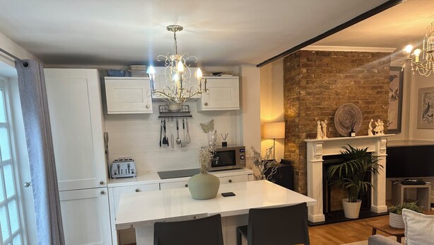 Uma cozinha moderna com uma ilha central, banquetas, um candelabro e uma lareira.