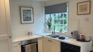 Cozinha compacta com lava-louças, forno e pia. Há uma janela com vista para o verde lá fora.
