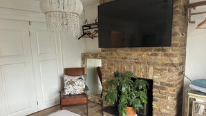 Quarto com lareira de tijolos, televisão na parede, lustre pendurado e planta em vaso.