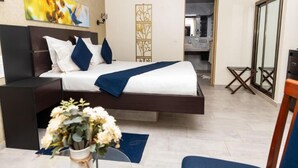 Quarto de hotel moderno com cama, mesas de cabeceira, um vaso de flores e vista para o banheiro.