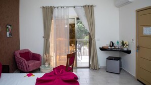 Quarto com cama, uma cadeira vermelha, uma mesa pequena com um vaso, uma cozinha compacta e uma porta de vidro que dá para uma área externa.