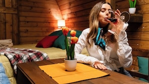 Interior acolhedor de uma cabana de madeira, com uma cama, uma mesa com um vaso de tulipas e uma pessoa sentada à mesa.