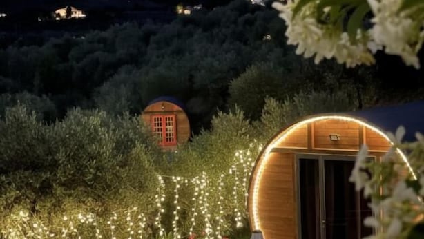 Estrutura de madeira com porta circular, cercada por um jardim com luzes de corda e vista para montanhas ao longe.