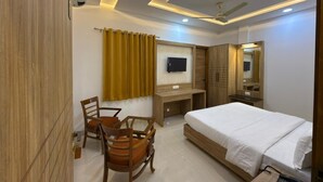 Quarto de hotel com cama, escrivaninha, cadeira, televisão e espelho.