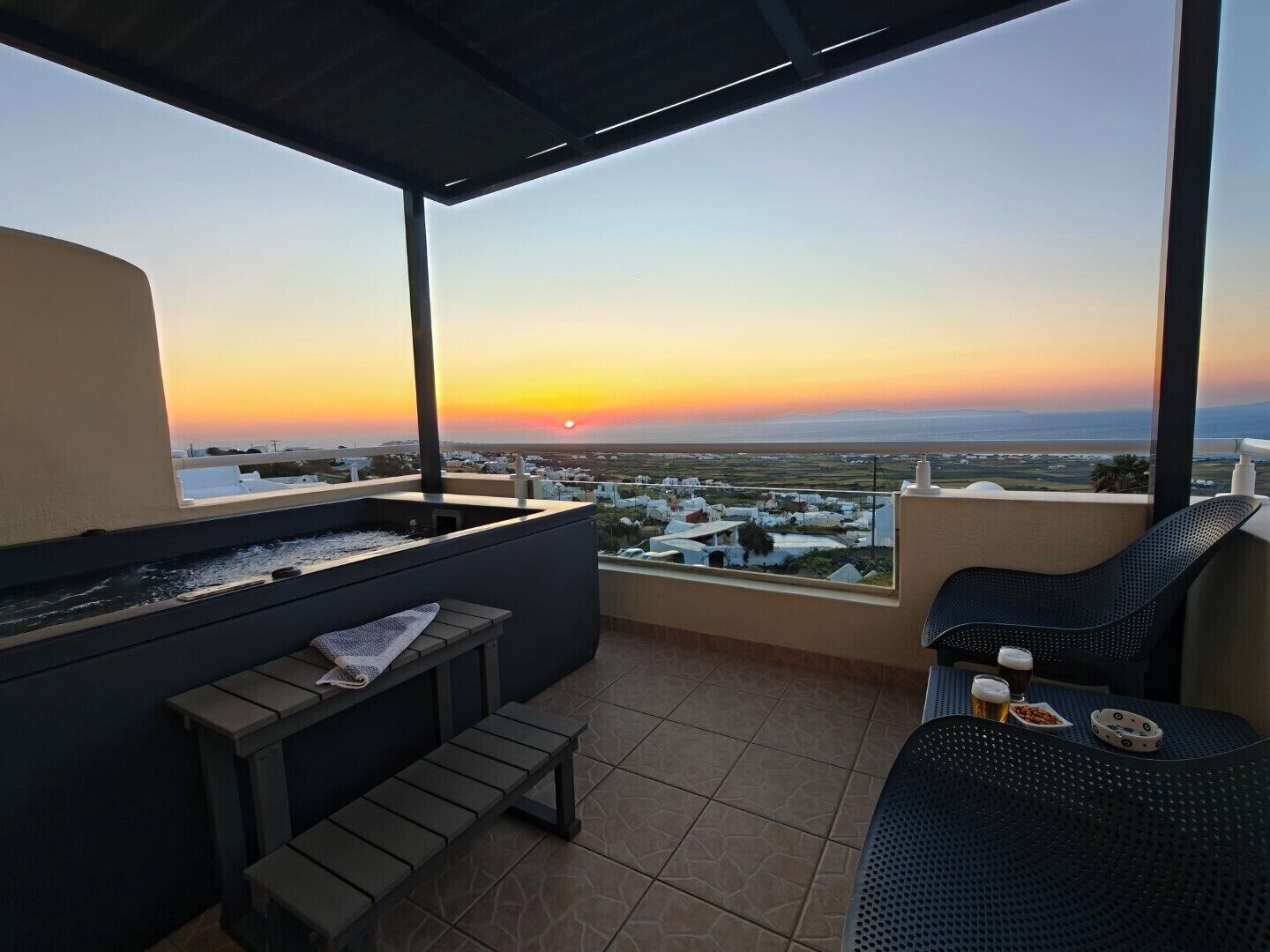 Varanda com hidromassagem, espaço para sentar e vista para o pôr do sol sobre uma cidade costeira.