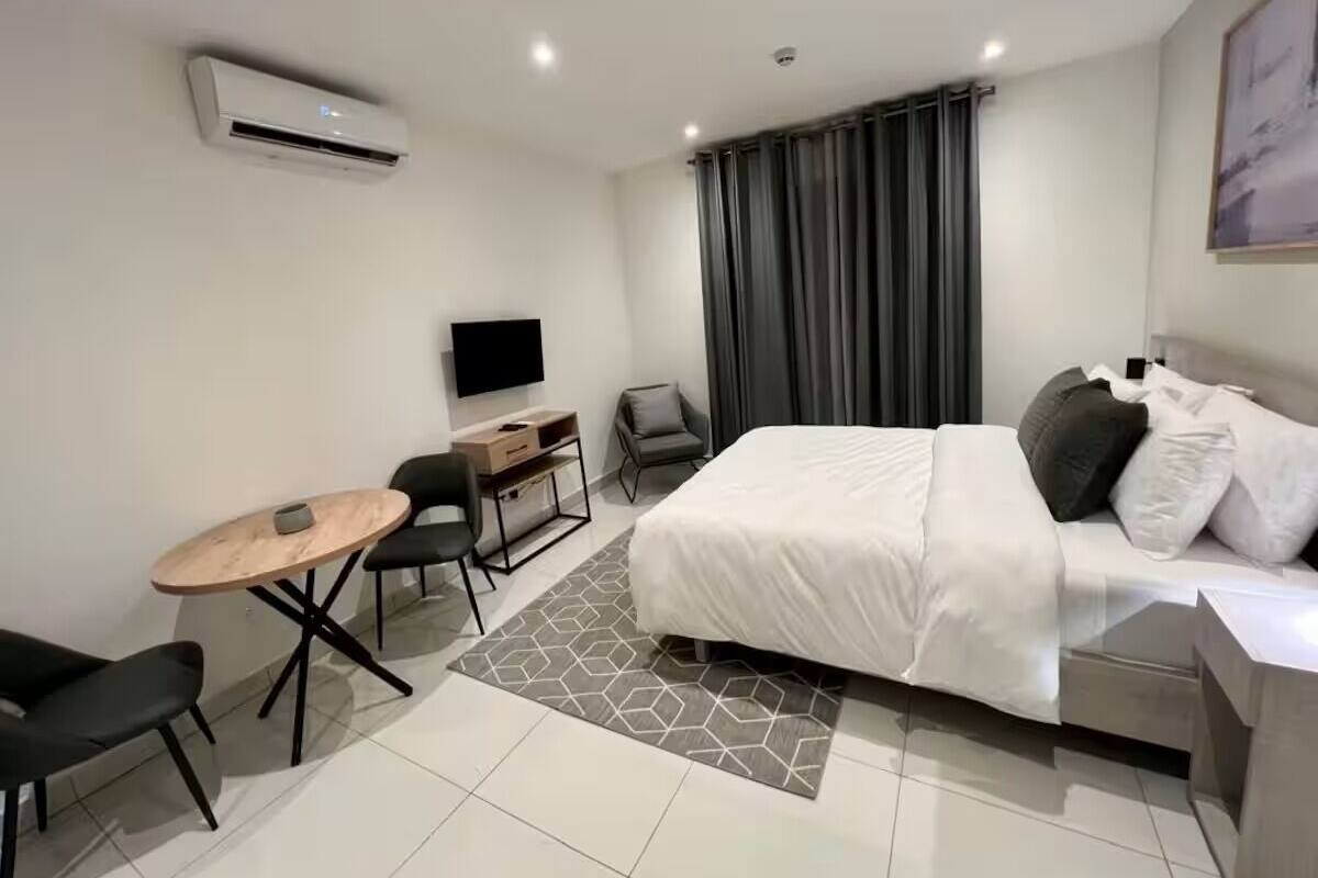 Quarto de hotel moderno com cama, escrivaninha, cadeira, televisão e aparelho de ar condicionado.