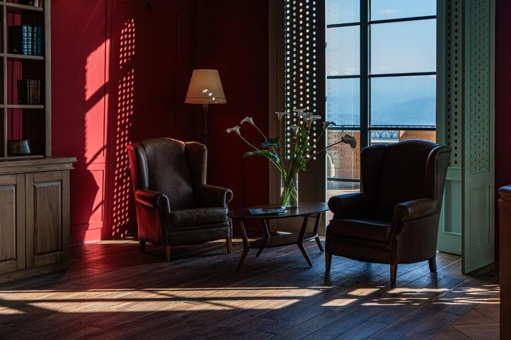 Quarto com duas poltronas de couro, uma mesa pequena, uma luminária e vista através de uma janela ampla.