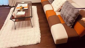 Sala de estar com sofá, mesa de centro de vidro, tapete branco e unidade de ar condicionado na parede.