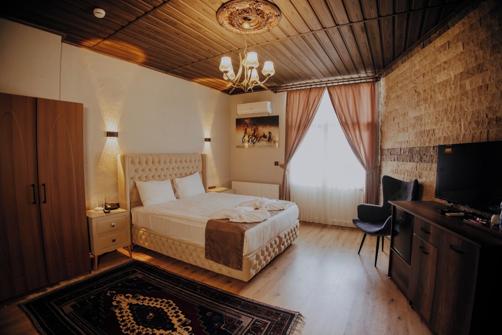 Quarto de hotel com uma cama grande, televisão, escrivaninha e uma cadeira.