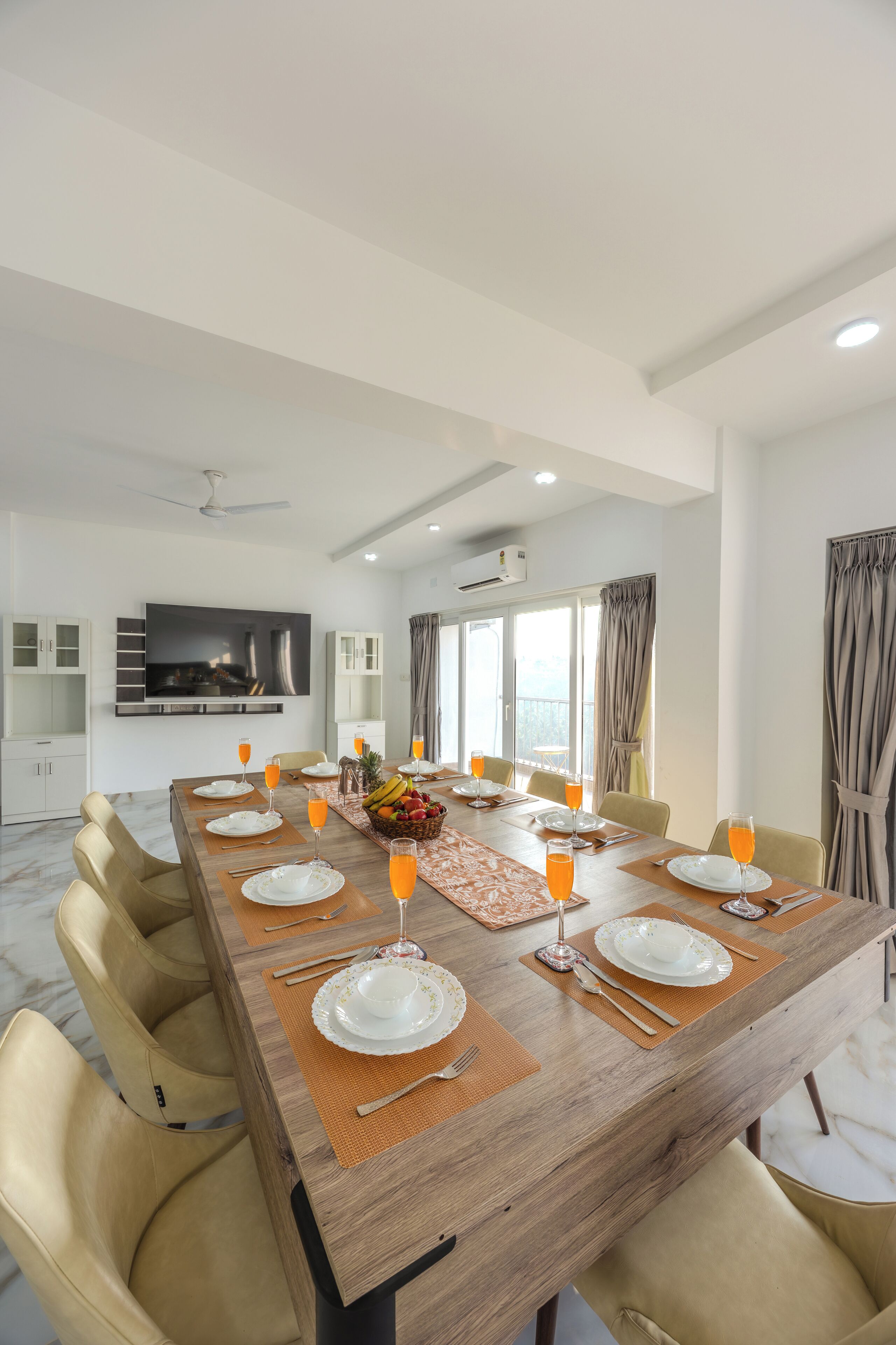Uma sala de jantar com uma longa mesa de madeira posta para seis pessoas, rodeada por cadeiras bege.
