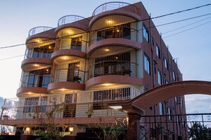 Um hotel com vários andares, varandas, grades e um detalhe arquitetônico curvo.
