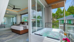 Quarto moderno com varanda envidraçada, banheira de vidro com pétalas de rosa e vista para o verde.