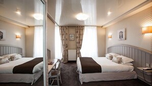 Quarto de hotel com duas camas, uma escrivaninha, uma cadeira e um espelho.