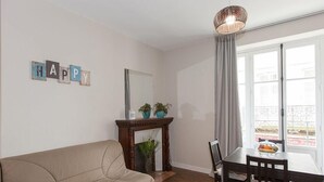 Uma sala de estar com sofá, lareira, mesa de jantar com cadeiras e janela com cortinas.