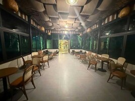 Um restaurante com área de estar central, mesas e cadeiras dispostas ao redor.