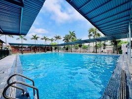 Piscina com área coberta, palmeiras e céu claro.
