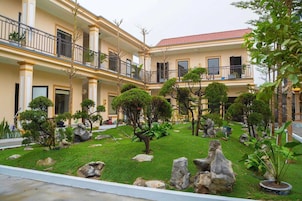 Pátio de hotel com gramado bem cuidado, jardim de pedras e um edifício de dois andares com varandas.