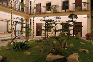 Edifício com vários níveis e um pátio ajardinado com bonsais e pedras.