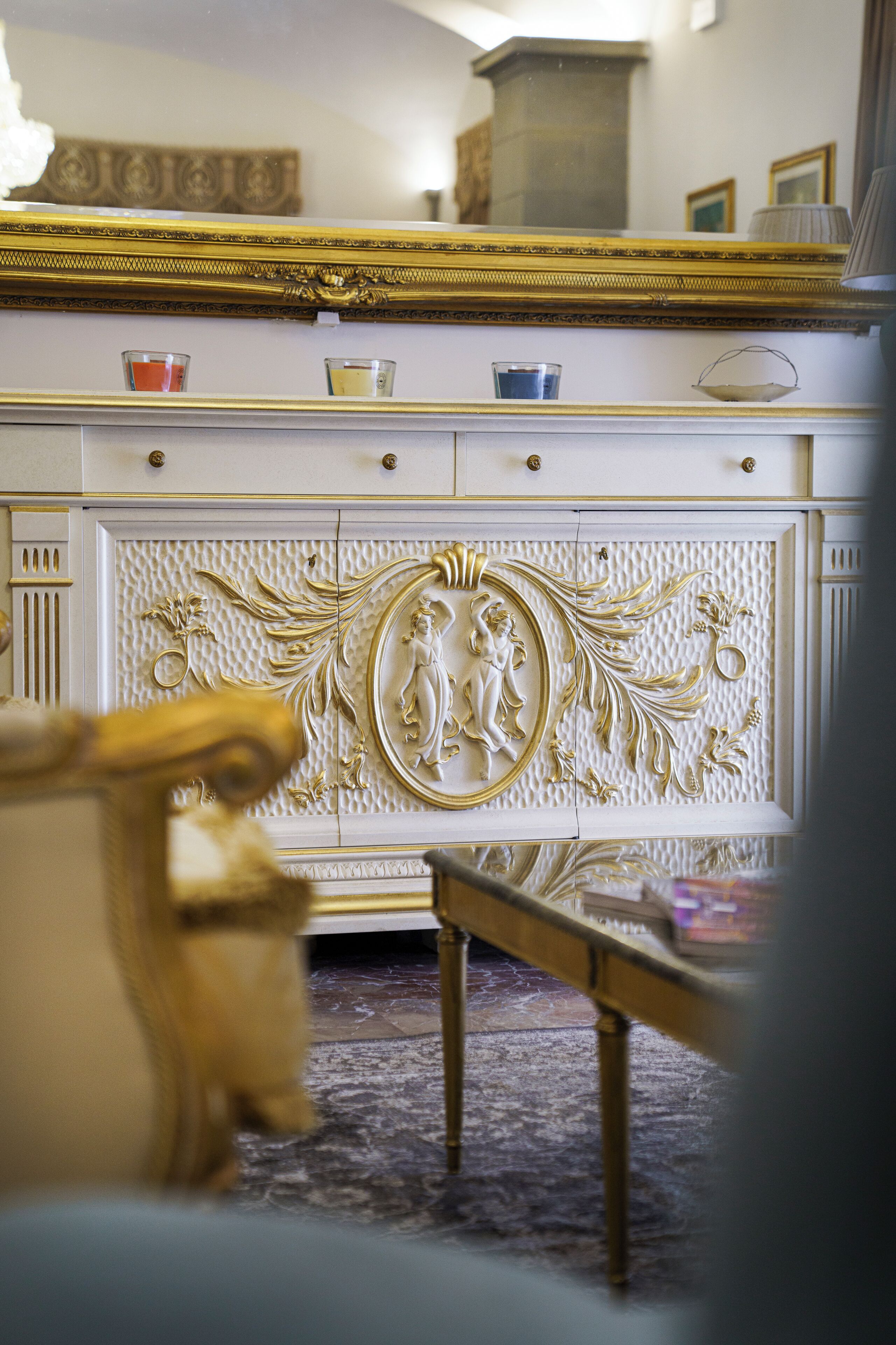 Um quarto com lareira branca e ornamentada, uma cadeira de madeira e uma mesa com abajur.