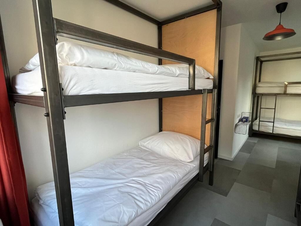 Quarto com beliche, cabeceira de madeira, cortina vermelha e uma pequena mesa com cesta.