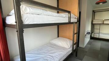 Quarto com beliche, cabeceira de madeira, cortina vermelha e uma pequena mesa com cesta.