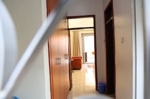 Um corredor leva a um quarto com uma porta de madeira, um balde azul e um sofá laranja.