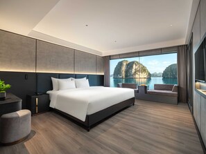 Quarto moderno com cama grande, mesas de cabeceira, área de estar e vista para uma paisagem montanhosa.
