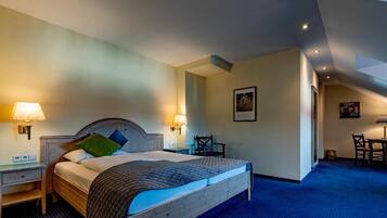 Quarto de hotel com uma cama grande, duas mesas de cabeceira com abajures, uma cadeira e uma mesinha.