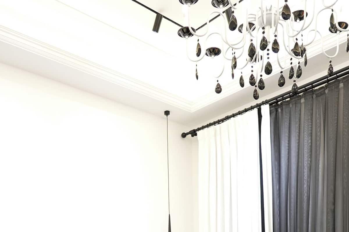 Quarto de hotel moderno com cabeceira preta, roupa de cama branca e um candelabro.