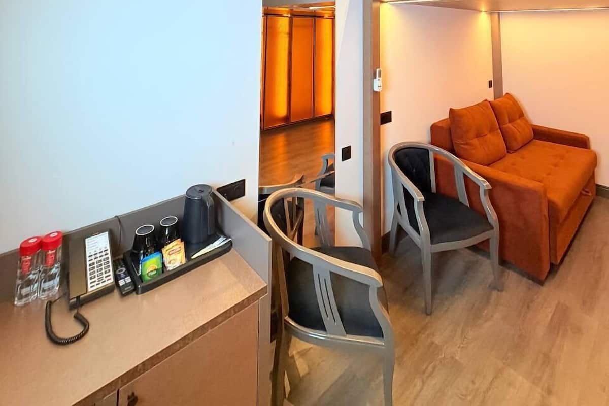 Quarto de hotel compacto com cozinha compacta, sofá, poltrona e pequena mesa de trabalho com telefone e amenities.