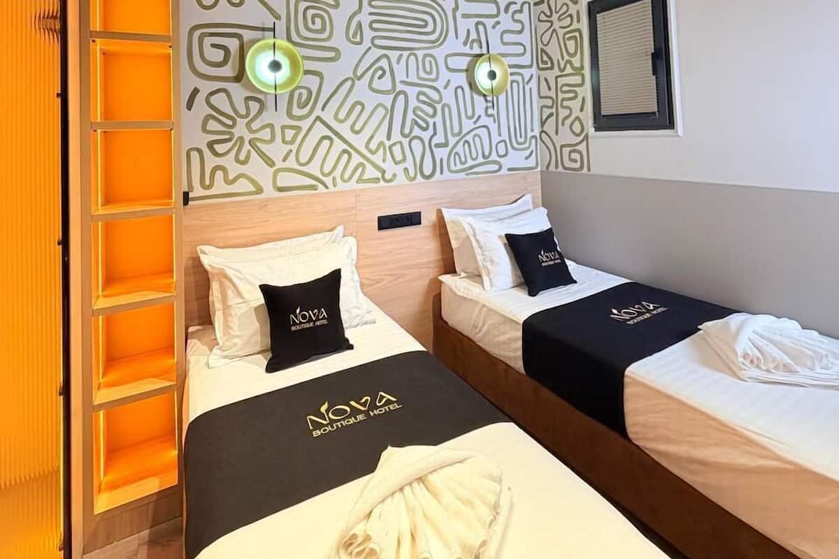 Quarto de hotel com duas camas, um guarda-roupa e um detalhe decorativo na parede.