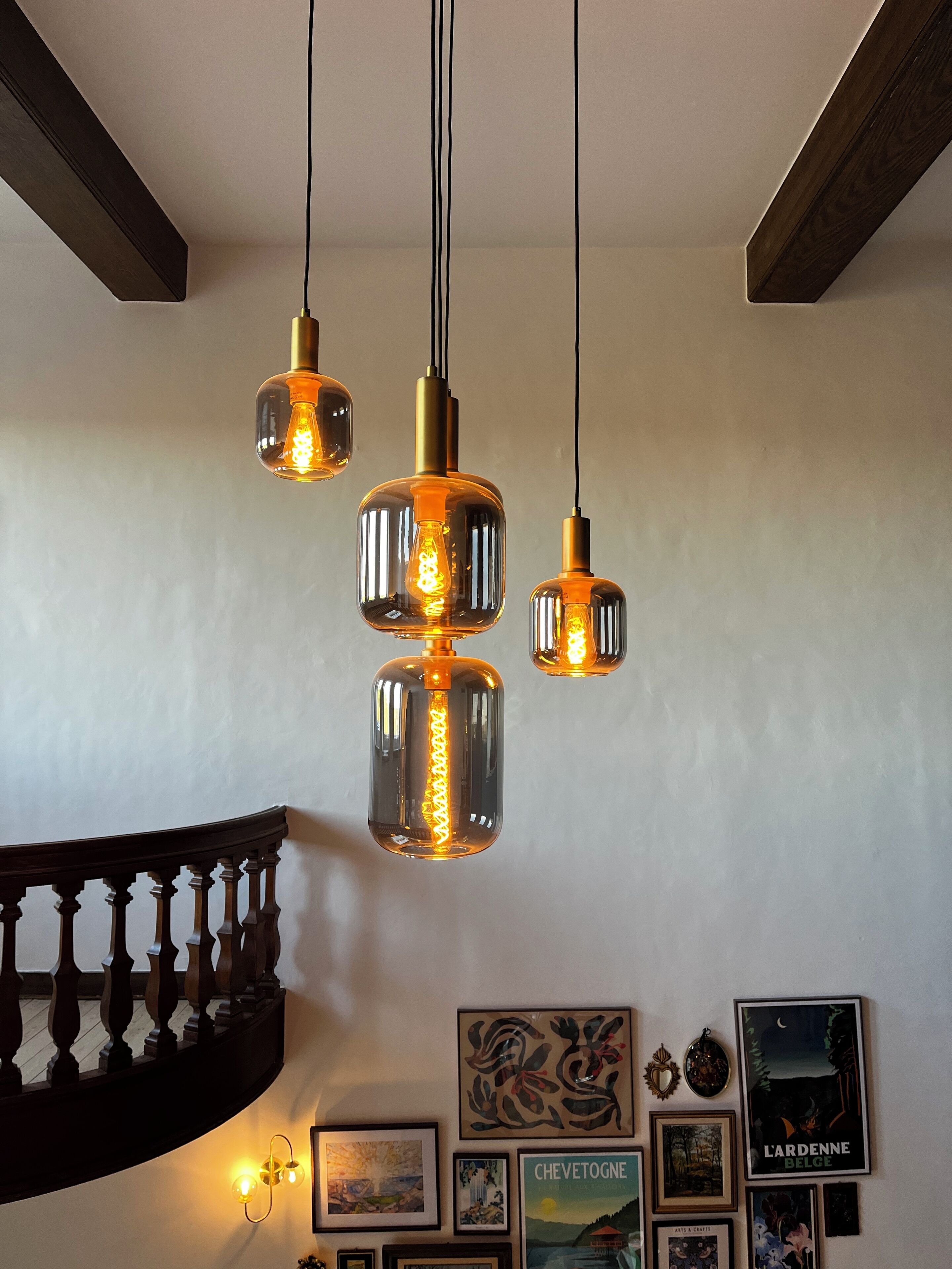 Quarto com escada de madeira, luminária fixada na parede com três lâmpadas e várias obras de arte emolduradas.