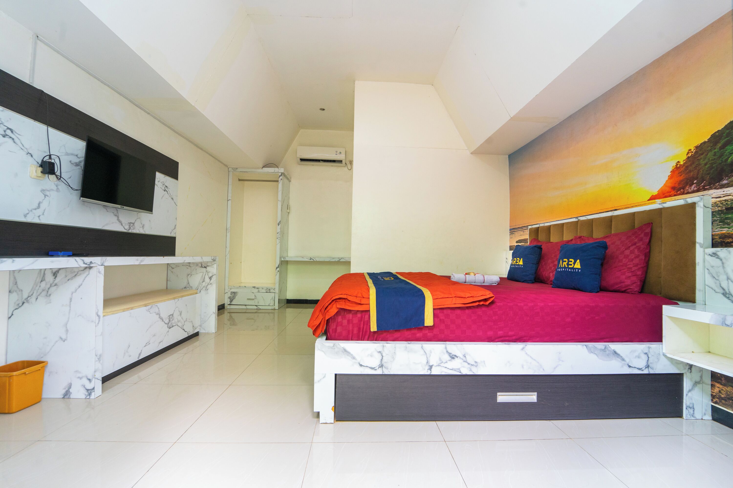 Quarto moderno com cama de mármore, televisão na parede e um mural com pôr do sol.