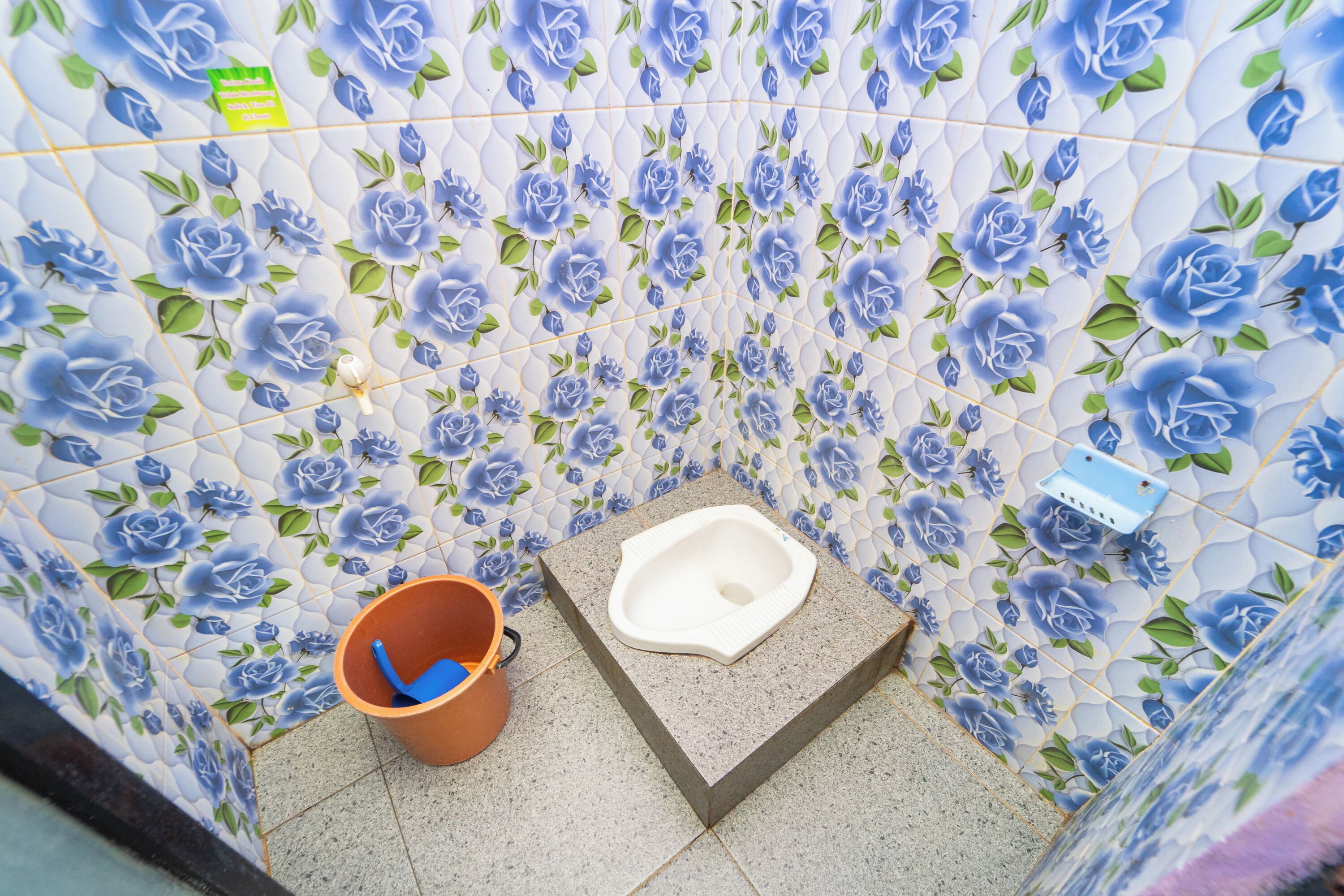 Casa de banho com sanita, um balde e parede com azulejos florais azuis.