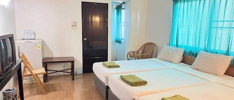 Quarto de hotel com duas camas, televisão, frigorífico, cadeira e janela com cortinas.
