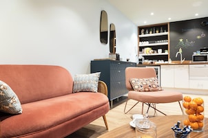 Sala de estar moderna com sofá, poltrona e mesa de centro. Há uma cozinha com armários e micro-ondas.