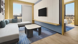 Uma sala de estar moderna com sofá, mesa de centro, TV de tela plana na parede e grandes janelas com vista para a cidade.