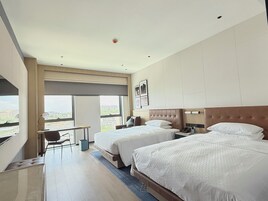 Quarto de hotel com duas camas, uma escrivaninha, uma cadeira, uma mesinha e vista para a cidade.