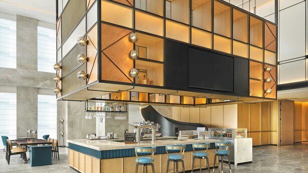 Uma área de bar moderna com balcão alto, banquetas e cozinha ao fundo.