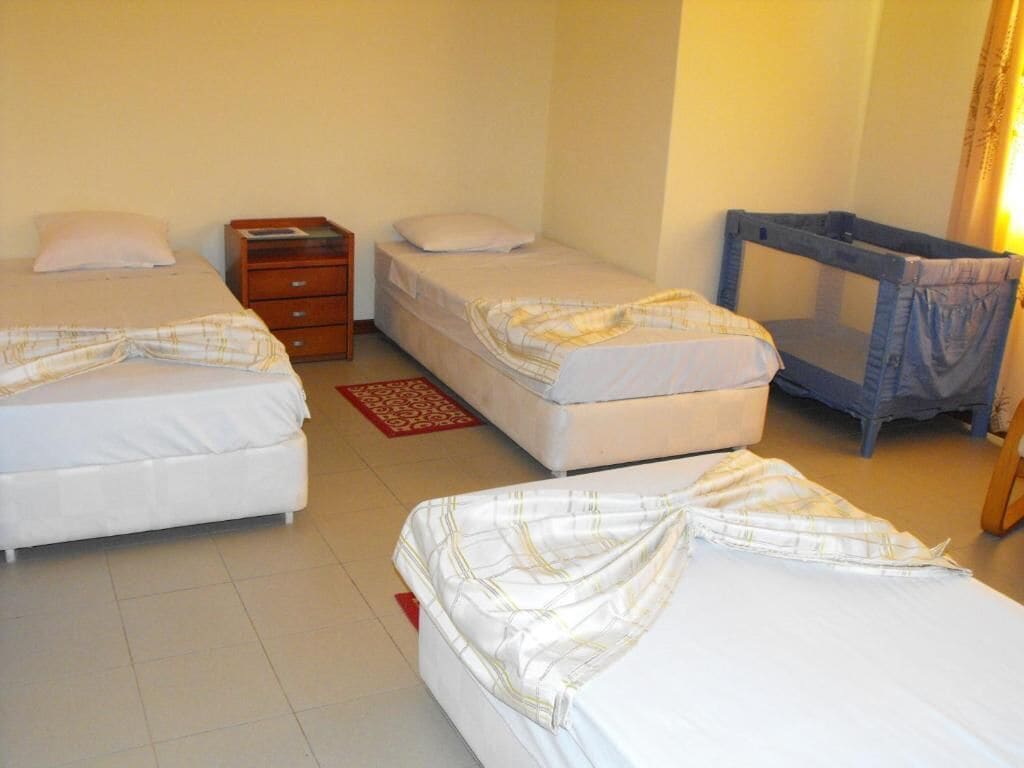 Quarto com três camas, um pequeno armário de madeira e um cercadinho azul.