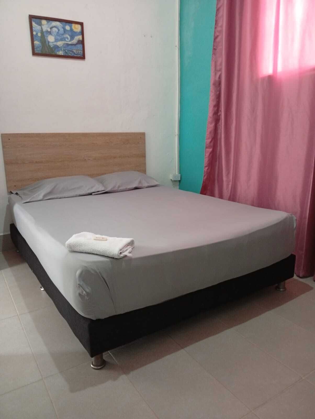 Uma cama de solteiro com cabeceira de madeira, roupa de cama cinza e uma toalha branca dobrada sobre a cama.